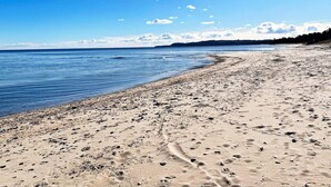 Uma praia com céu claro, água calma e pegadas na areia.