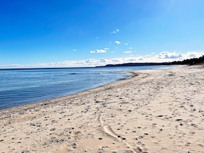 Uma praia com céu claro, água calma e pegadas na areia.