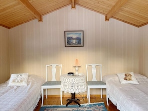 Quarto aconchegante com duas camas de solteiro, uma mesa pequena com abajur e um quadro na parede.