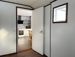 Corredor estreito que dá para uma cozinha com armários brancos, micro-ondas e fogão.