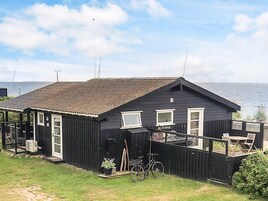 Uma casa de madeira à beira-mar com varanda, uma bicicleta e vista para o mar.