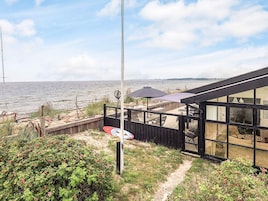 Uma propriedade costeira com varanda e vista para o mar, com mobiliário de exterior e uma sala envidraçada.