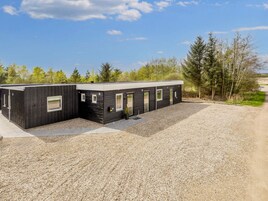 Um edifício moderno térreo com entrada por um caminho de cascalho e uma área verde ao fundo.