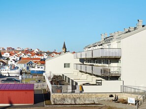 Um edifício de vários andares com varandas, uma escadaria e vista para uma cidade com casas de telhado vermelho ao fundo.
