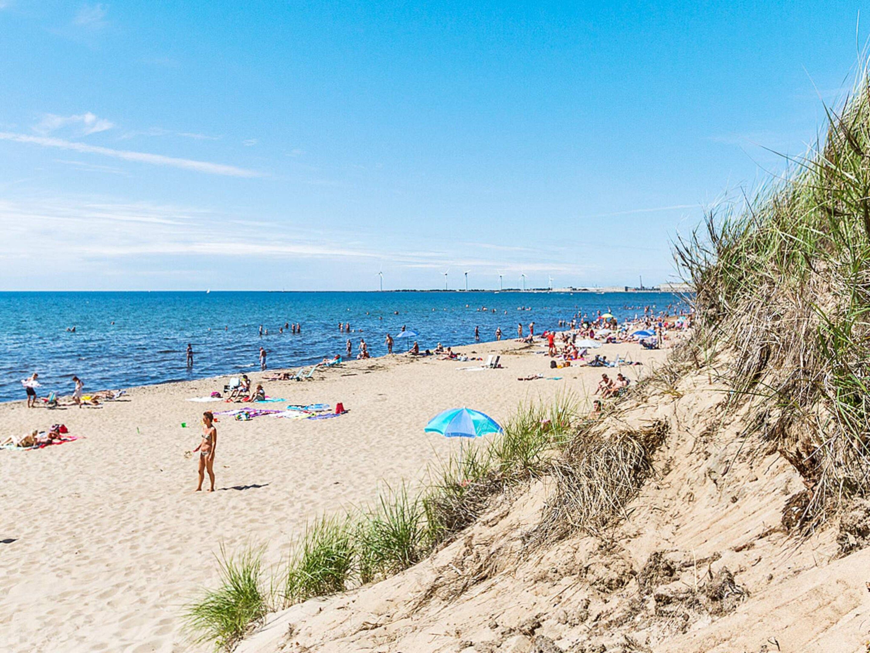 Uma praia com pessoas se banhando e tomando sol, uma faixa de areia e um céu azul límpido.