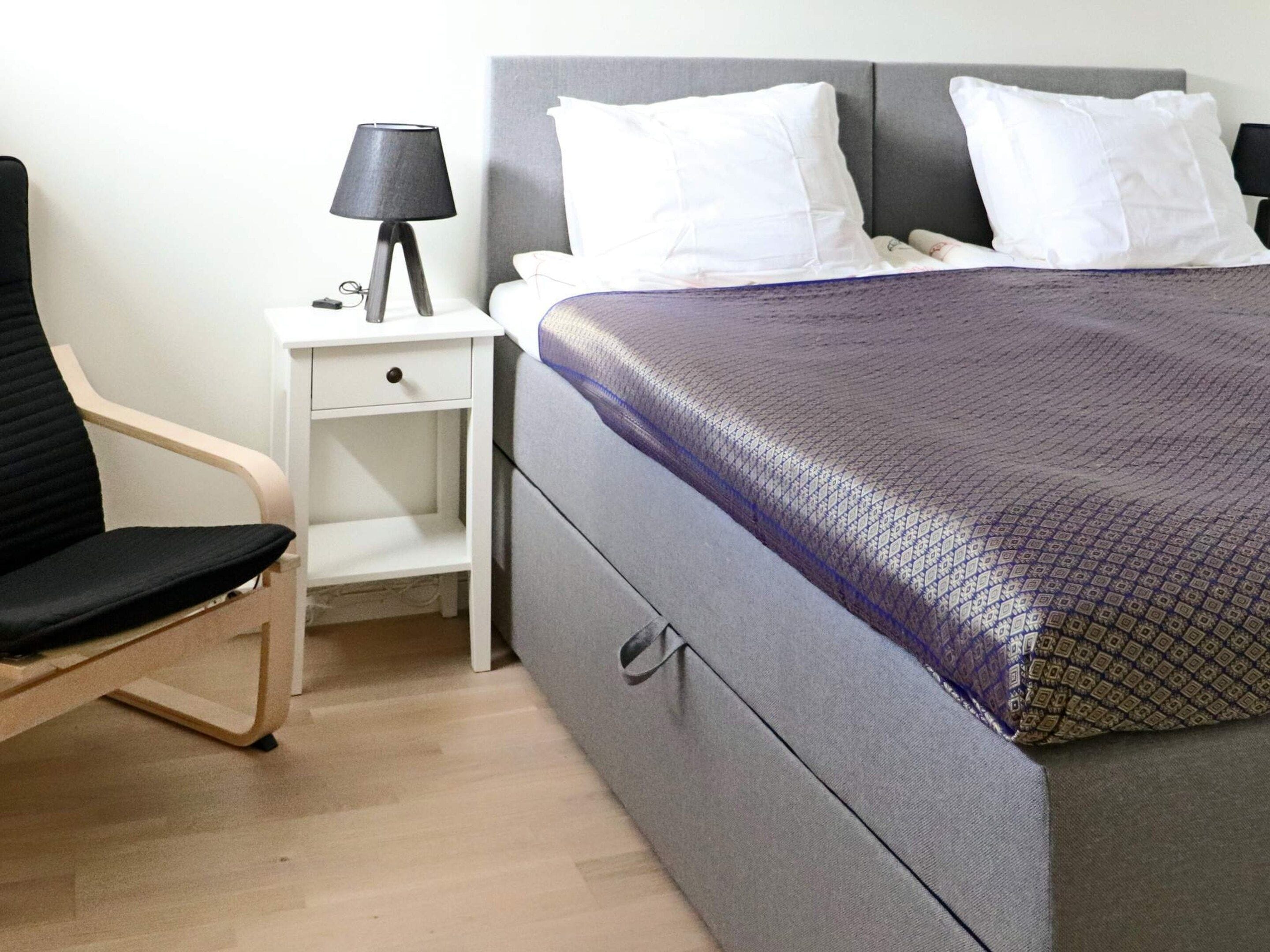 Quarto com cama, mesa de cabeceira com abajur e uma cadeira.