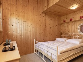 Quarto com painéis de madeira, uma cama, uma mesinha de cabeceira e um espelho fixado na parede.