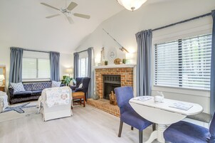Uma sala de estar aconchegante com lareira, ventilador de teto e um espaço de jantar com cadeiras azuis.