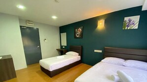 Quarto de hotel com duas camas, piso de madeira, uma parede de destaque verde escuro e uma escrivaninha pequena.