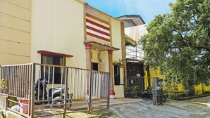 Um edifício com fachada amarela, portão de metal e uma árvore em primeiro plano.