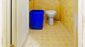 Um banheiro pequeno com azulejos amarelos estampados, vaso sanitário branco e lixeira azul.