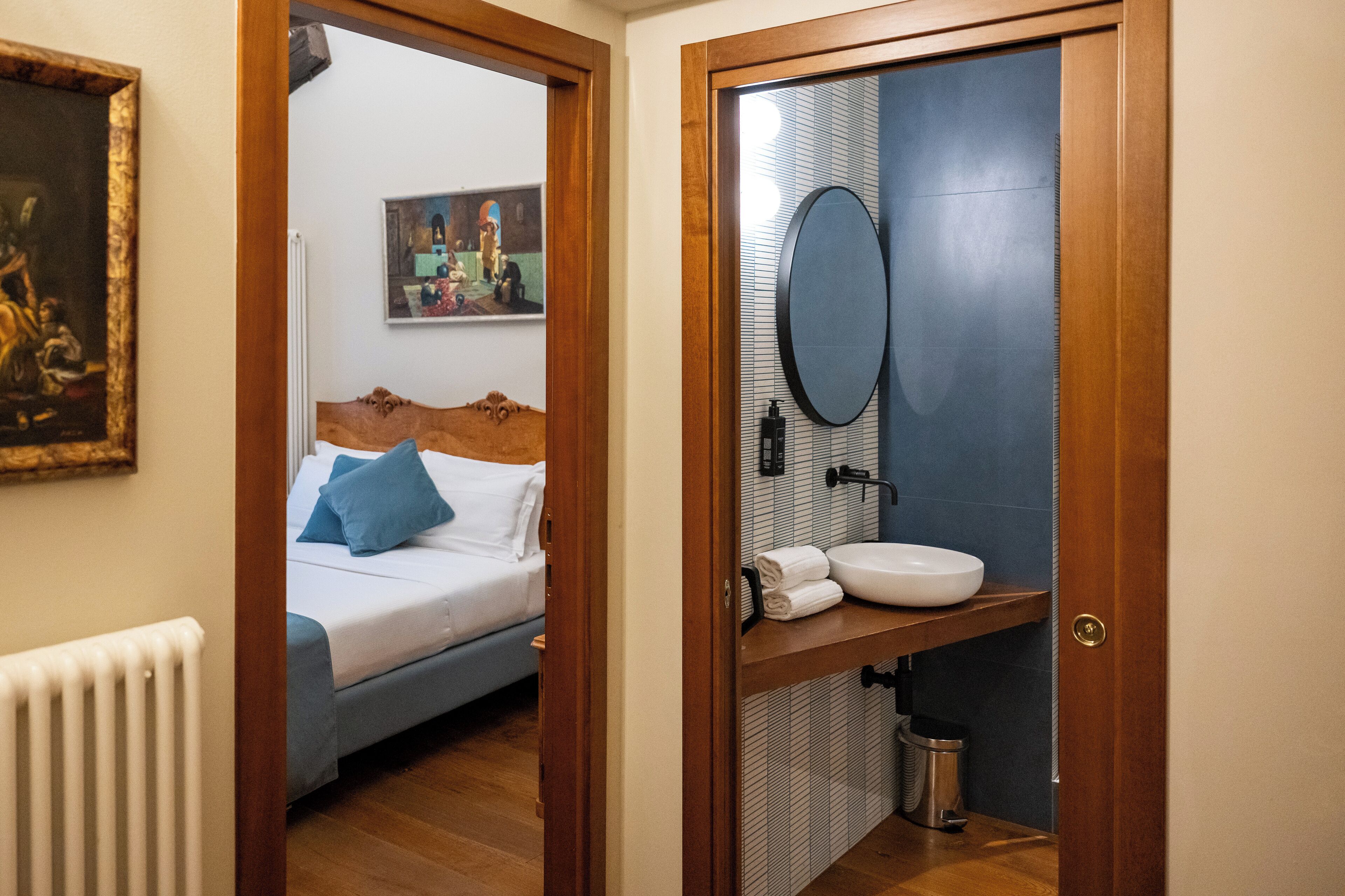 Quarto com cama, mesa de cabeceira, espelho e banheiro com pia e vaso sanitário.