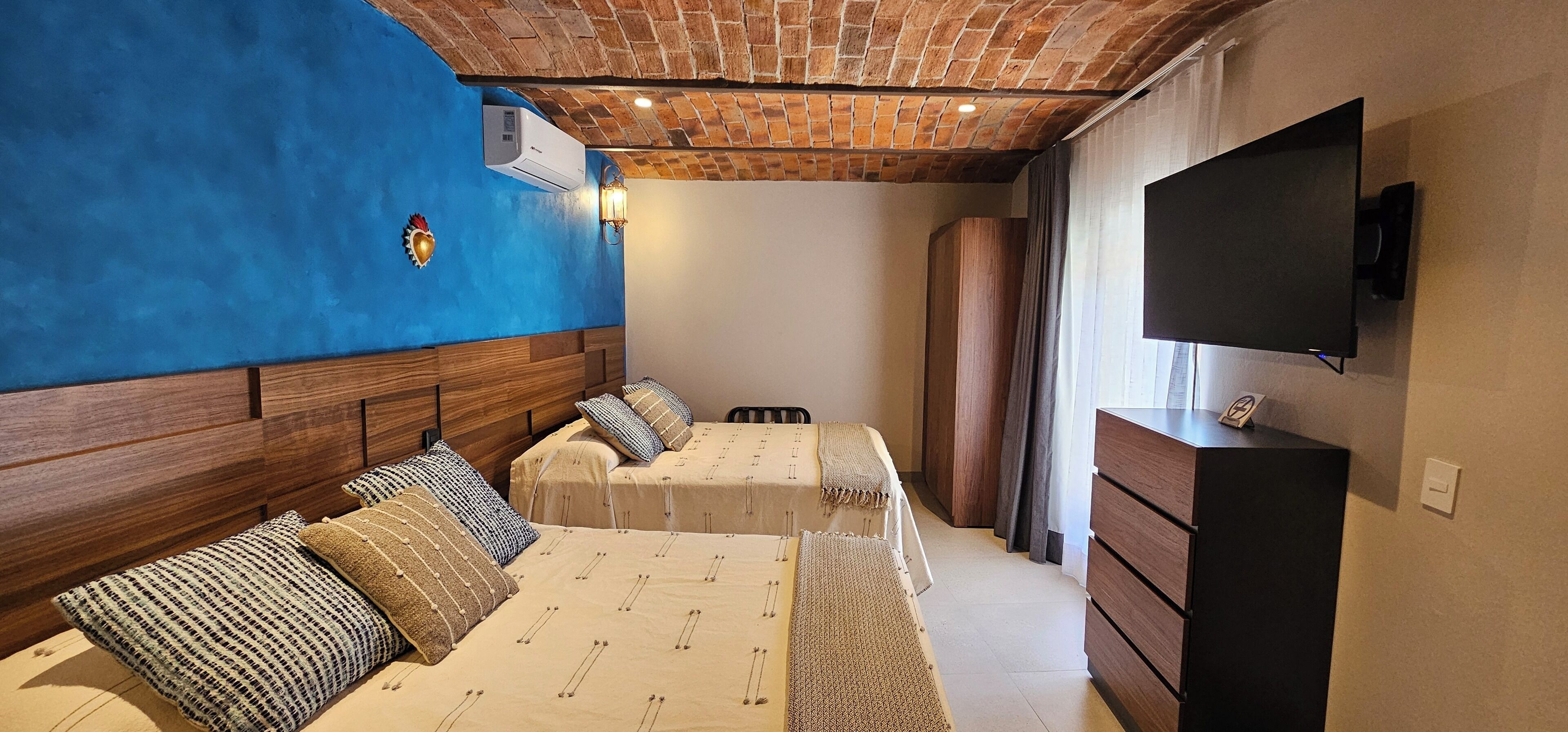 Quarto de hotel com duas camas, televisão de tela plana, cômoda de madeira e teto de tijolos.