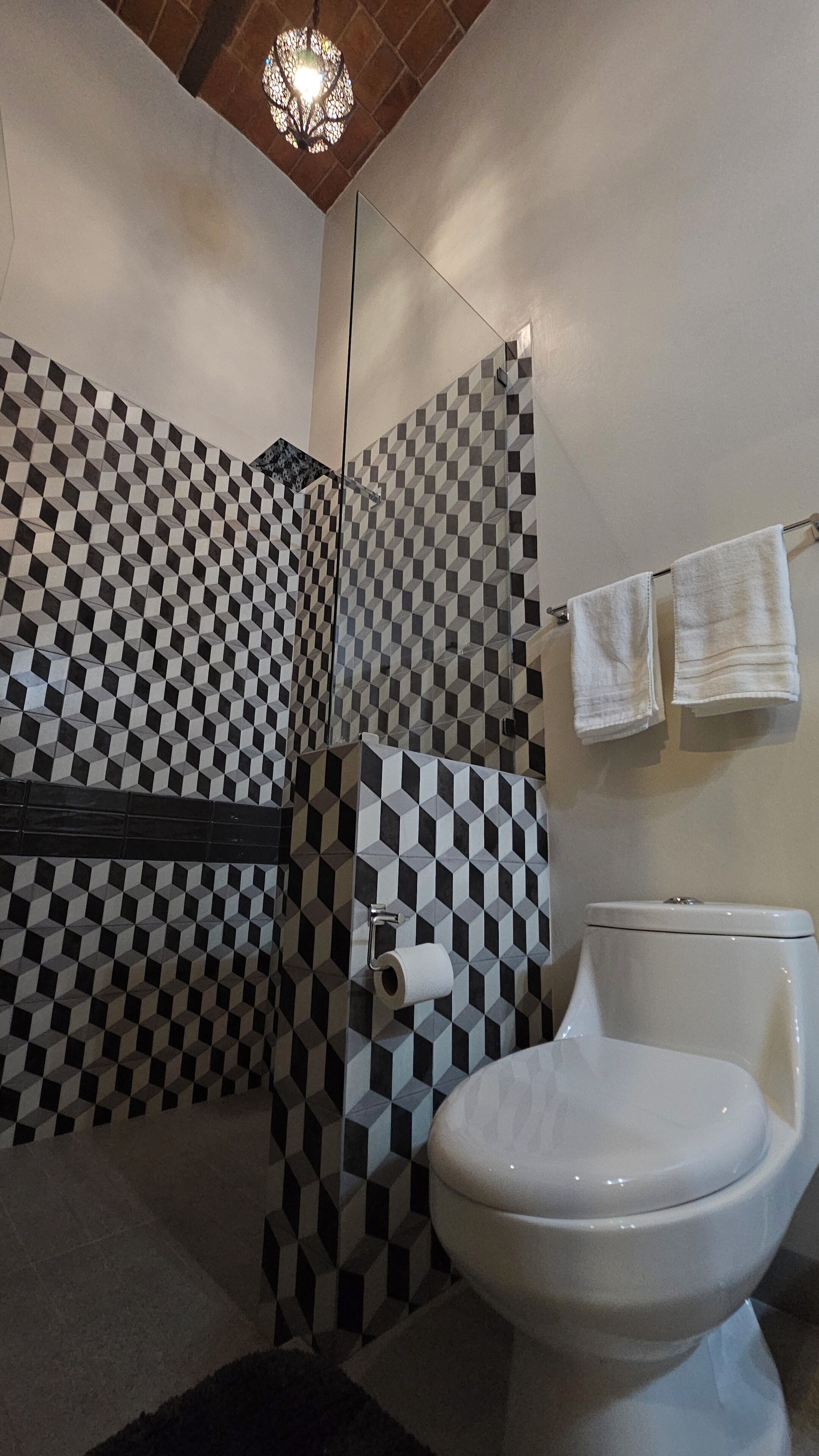 Um banheiro com parede de azulejos quadriculada, vaso sanitário e porta-toalhas com toalhas.