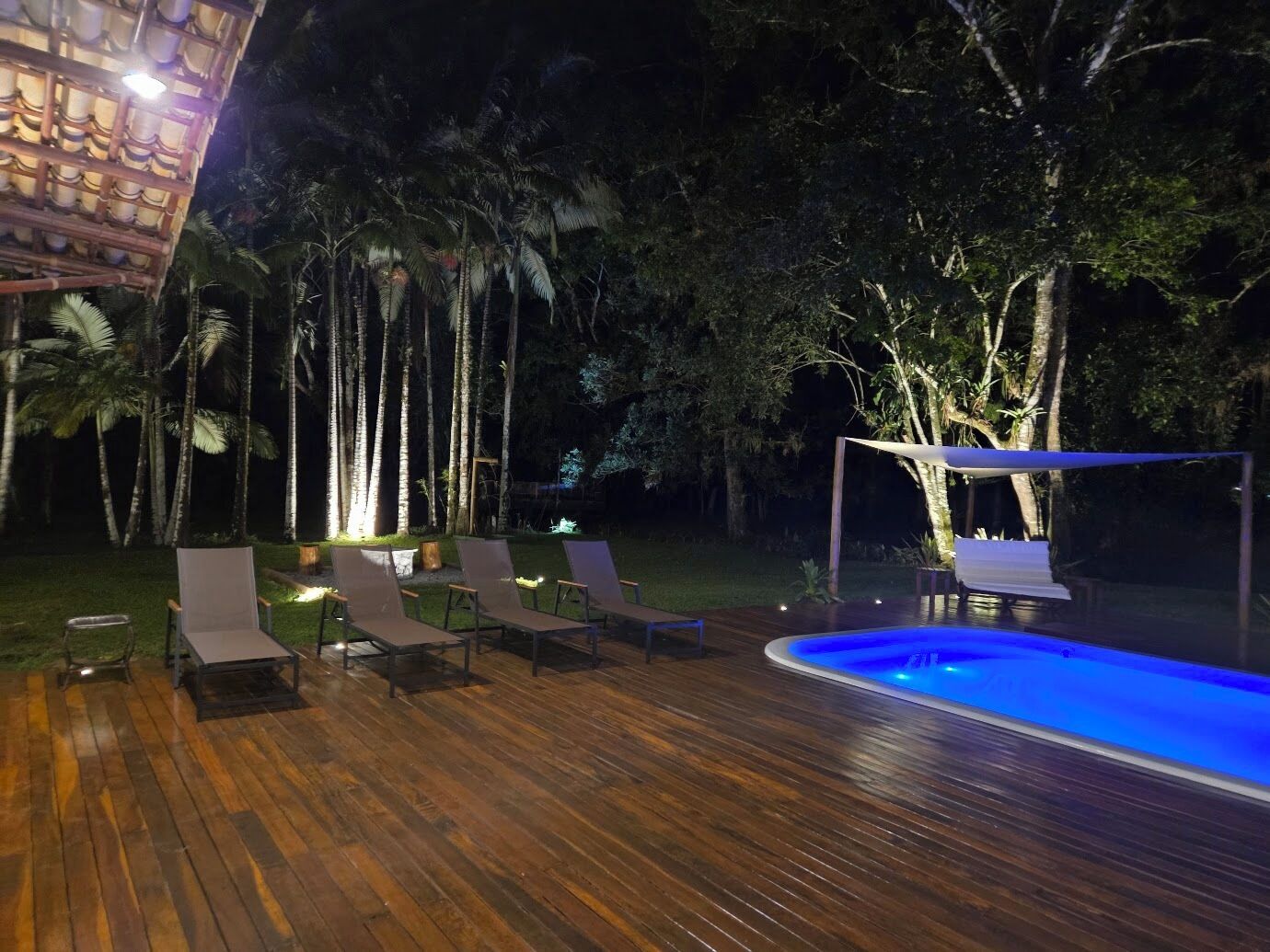 Um deck de madeira com espreguiçadeiras e uma piscina à noite.