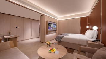 Quarto de hotel moderno com uma cama, uma mesa de escritório, uma mesa redonda com frutas e uma TV na parede.