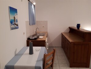 Cozinha compacta com pia, fogão e bancada de madeira. Uma mesa com toalha azul e um vaso em primeiro plano.