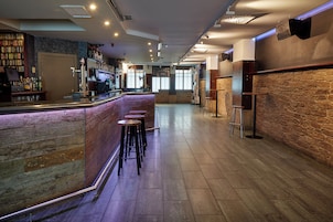 Uma área de bar com balcão, banquetas e uma estante com diversos objetos.