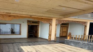 Uma sala de estar integrada, com teto e piso de madeira, portas de madeira e uma varanda com balaústres de pedra.