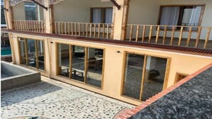 Um edifício de dois andares com varanda, janelas amplas e um pátio com piso de azulejos.