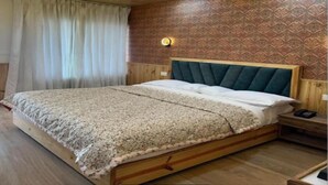 Quarto com teto de madeira, papel de parede estampado, cama com cabeceira verde, mesa de cabeceira e apoio para luminária.