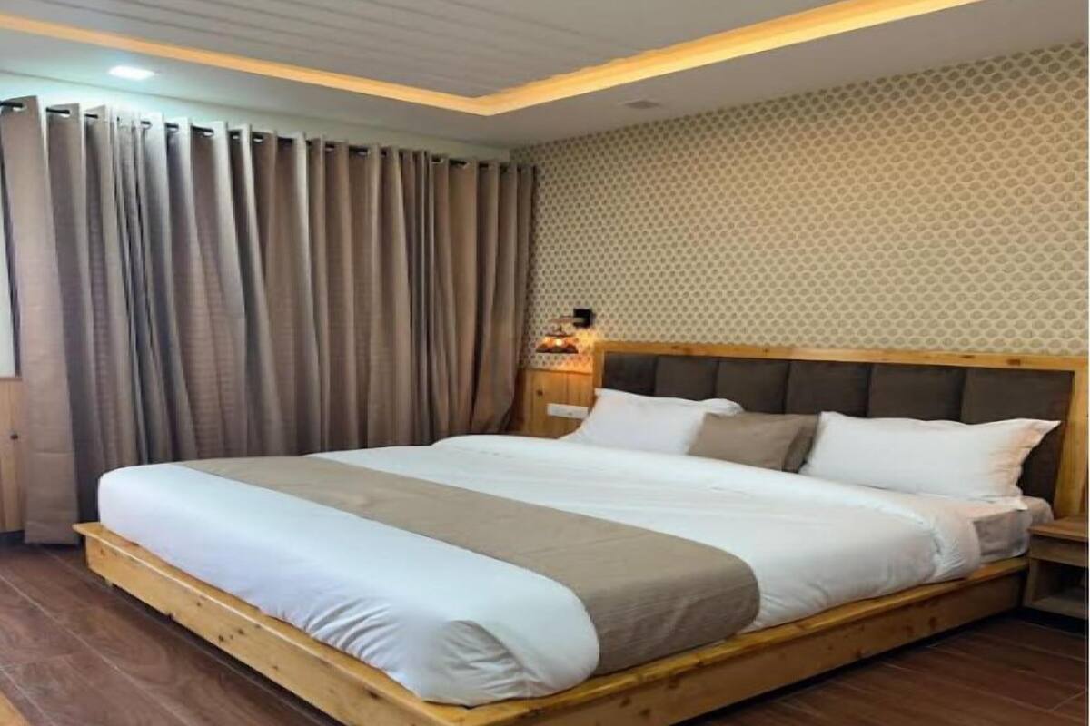 Quarto com estrutura de cama de madeira, roupa de cama branca e parede estampada.