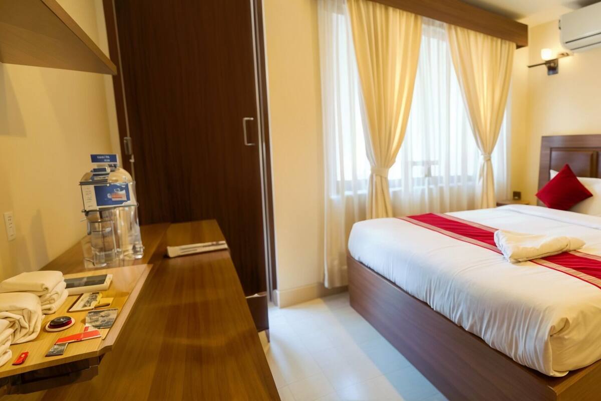 Quarto de hotel com cama, mesa de cabeceira e escrivaninha com dispensador de água e telefone.