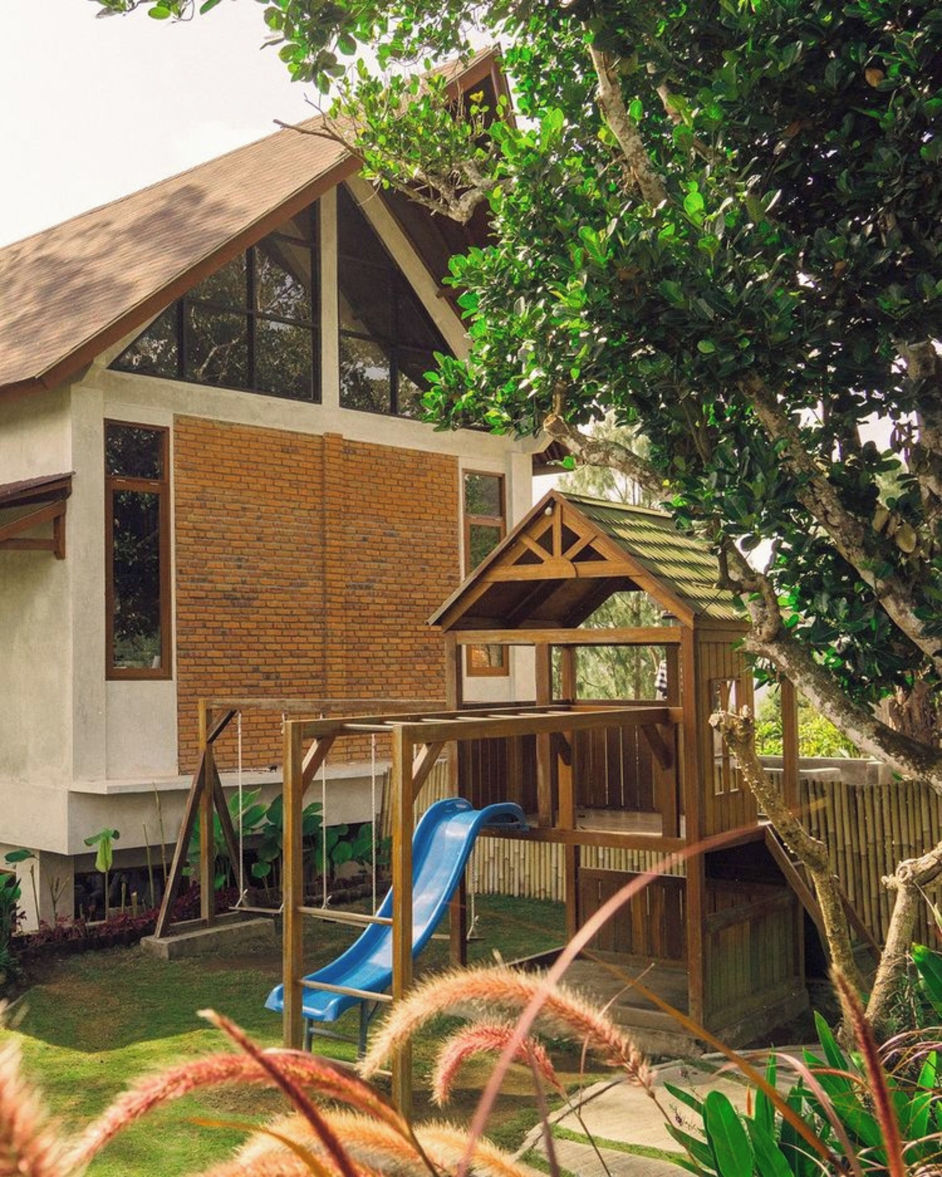 Uma casa moderna com um grande muro de tijolos, um parquinho de madeira e um escorrega azul no quintal.