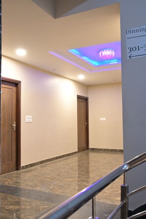 Um corredor com piso de mármore, portas de madeira e teto com iluminação azul.
