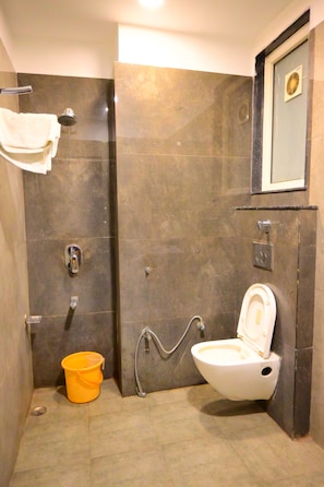 Casa de banho com chuveiro, sanita e um balde amarelo.