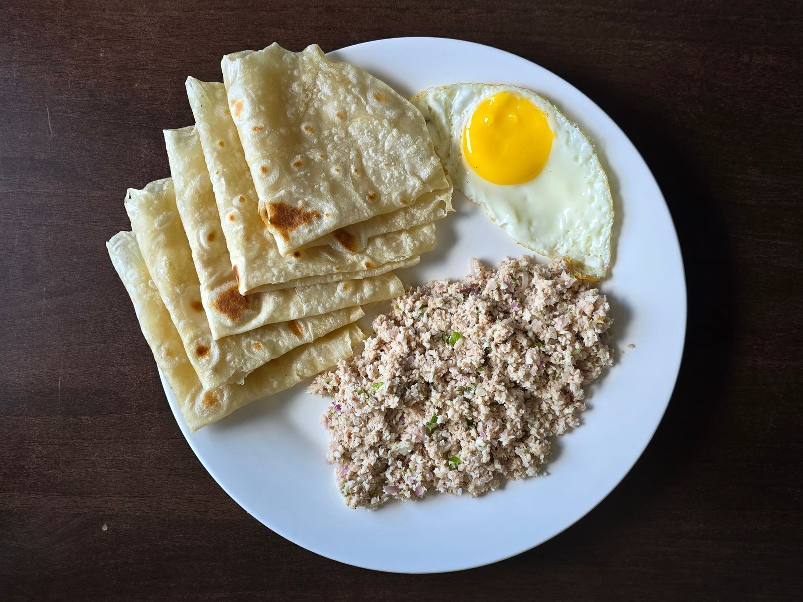 Um prato com vários crepes enrolados, um ovo frito e uma porção de carne moída.