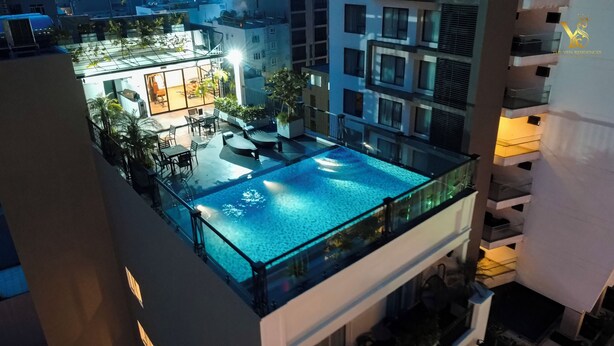 Piscina no terraço com guarda-corpos de vidro, cercada por área de estar ao ar livre e plantas.