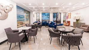 Um hall de hotel moderno com área de estar, um mural com cena de praia e uma grande janela com vista para o exterior.