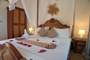 Quarto de hotel com cama grande, cabeceira de madeira, duas luminárias de apoio e um objeto decorativo na parede.