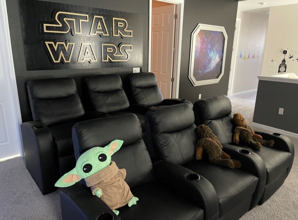 Sala de cinema com parede temática de Star Wars, poltronas de couro reclináveis e brinquedos de pelúcia.