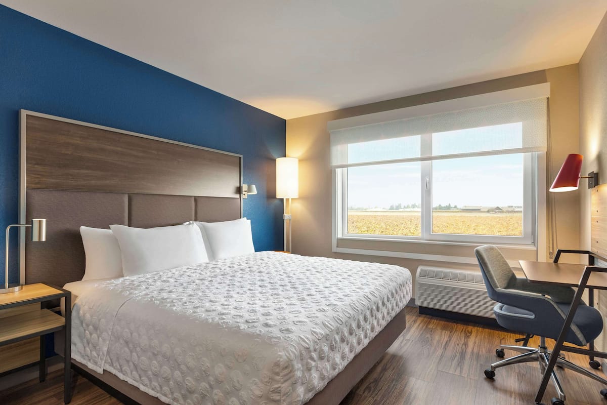 Quarto de hotel com uma cama grande, uma escrivaninha, uma cadeira, uma janela com vista para o campo e um aquecedor sob a cama.