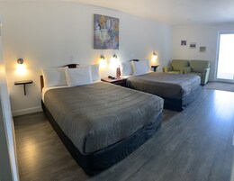 Quarto de hotel com duas camas, um quadro na parede, uma cadeira e um abajur.