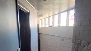 Um corredor estreito com piso de madeira, parede de tijolos brancos e porta preta.