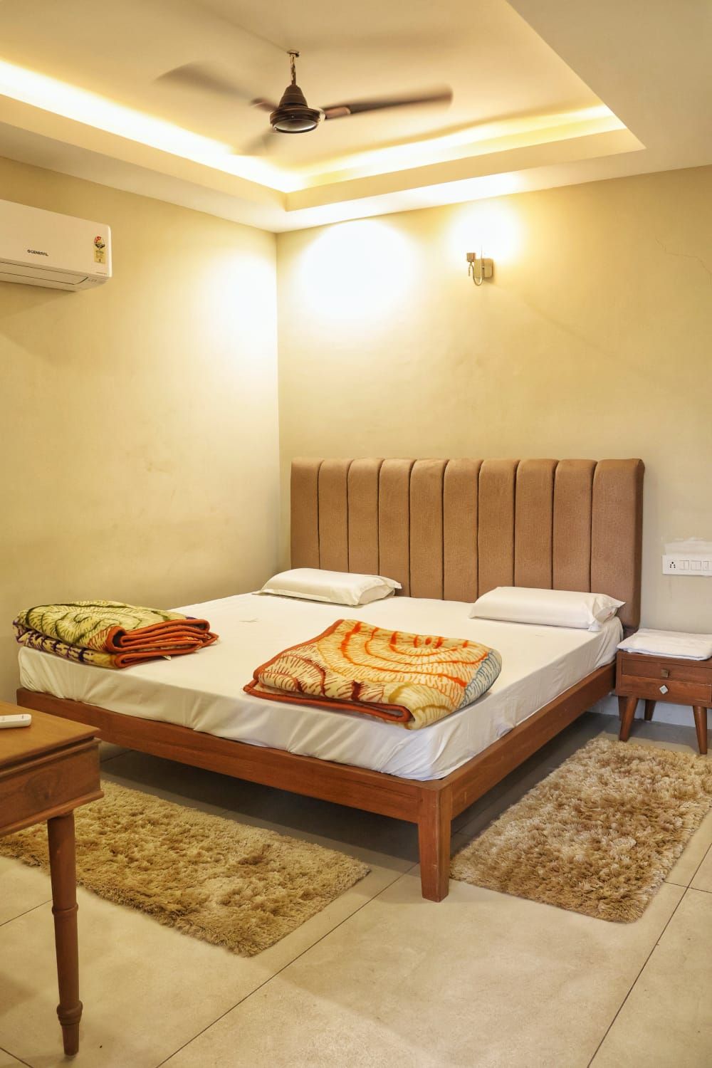 Quarto com cama de madeira, ventoinha no teto, ar condicionado e mesa de cabeceira.