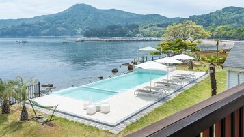 Uma piscina com espreguiçadeiras, vista para o mar e montanhas ao fundo.