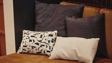 Um sofá marrom com três almofadas: uma estampada, uma branca lisa e uma cinza escura.