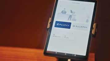 Um tablet apoiado em um suporte, exibindo um aplicativo japonês com ícones e texto.