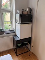 Uma cozinha compacta com micro-ondas, geladeira e cafeteira em uma prateleira de metal preto.