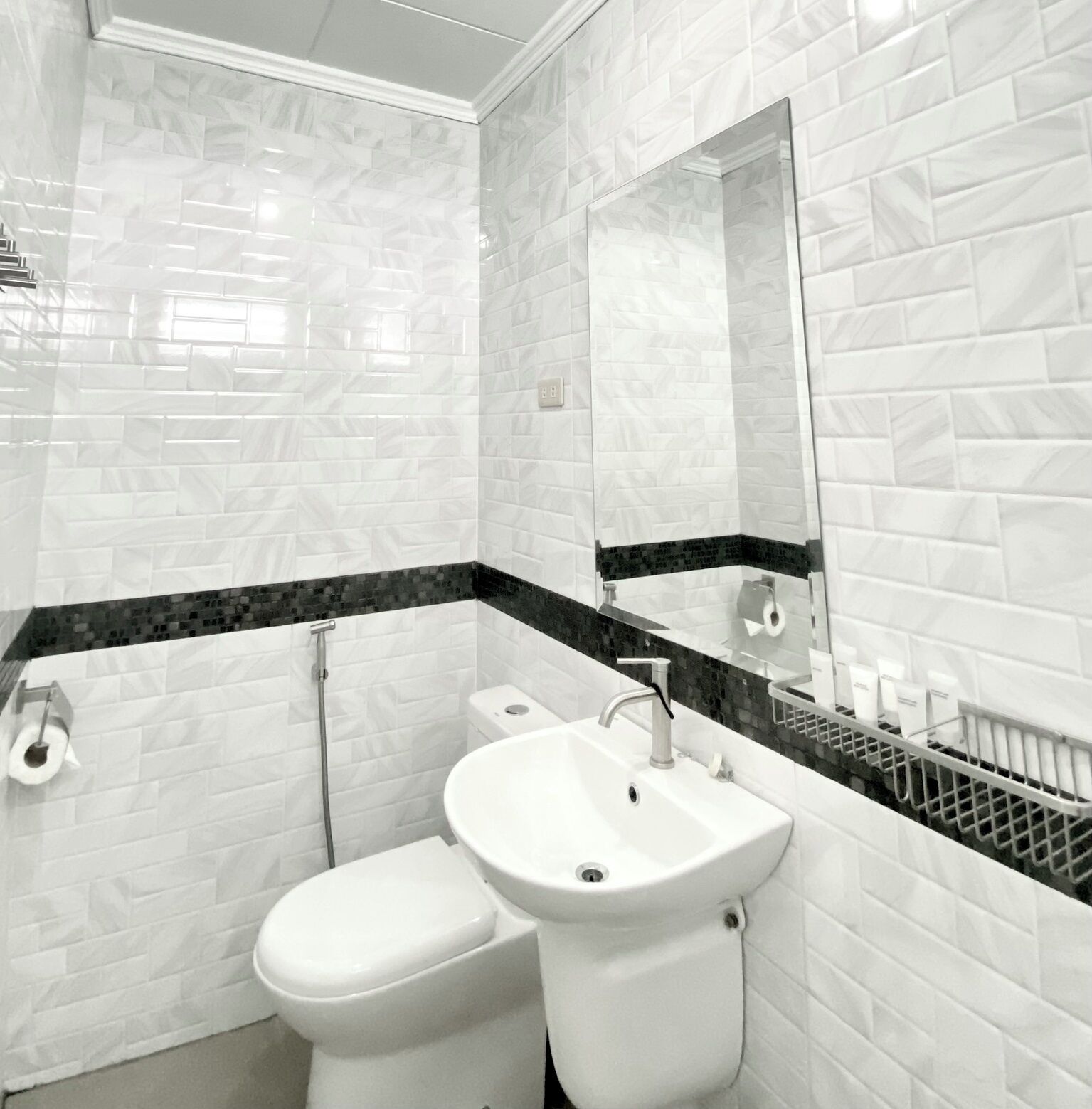 Casa de banho com azulejos brancos estilo metrô, bancada preta e branca, pia branca e sanita.
