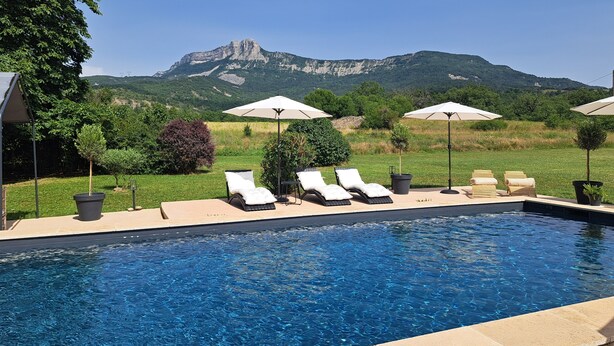 Área de piscina com espreguiçadeiras e guarda-sóis, rodeada por vegetação e vista para a montanha.