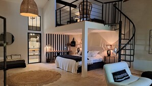 Quarto moderno com cama, mesas de cabeceira, uma cadeira, escada e luminária suspensa.