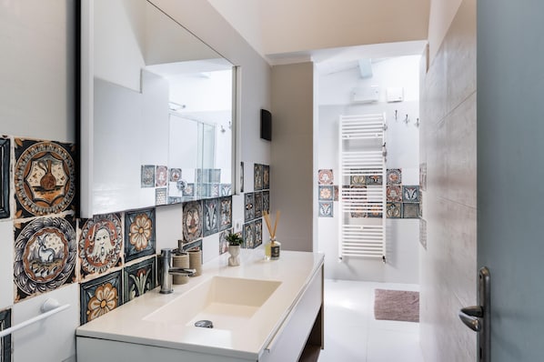 Uma casa de banho moderna com um espelho grande, uma sanita branca e azulejos decorativos.