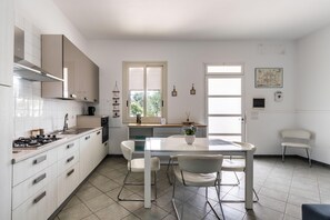 Uma cozinha moderna com armários brancos, fogão a gás e uma área de jantar com mesa e cadeiras brancas.