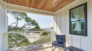 Um deck de madeira com vista para a praia, uma cadeira de vime e uma mesa.