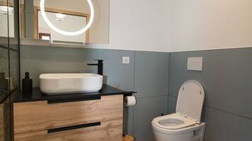 Um banheiro moderno com toucador de madeira, pia branca, vaso sanitário e espelho com iluminação circular.